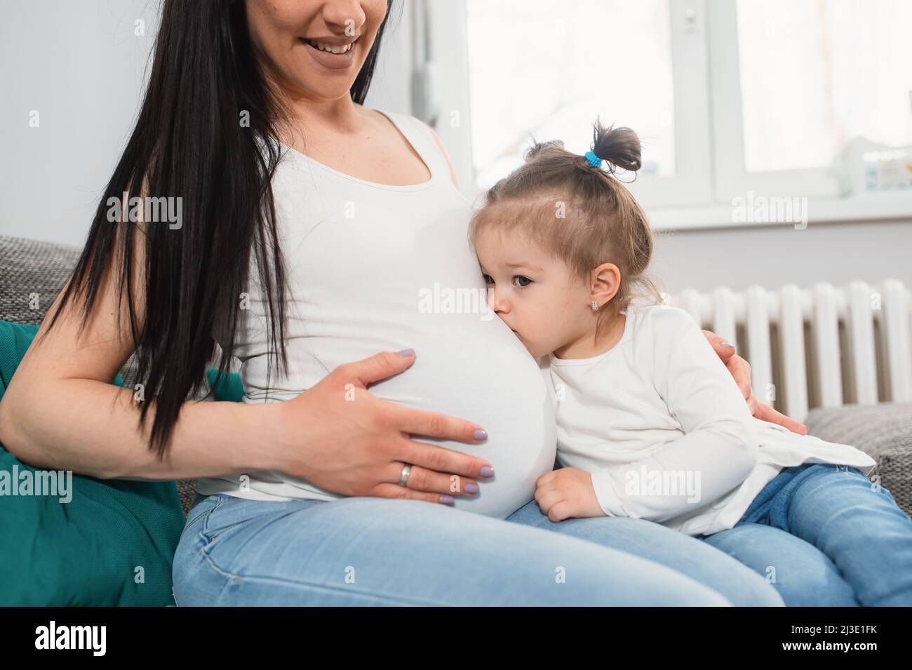 Mother and daughter hug on the sofa while a little girl with pigtails ...