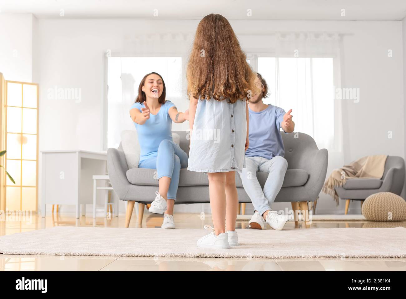Little daughter standing opposite her parents sitting on sofa Stock ...