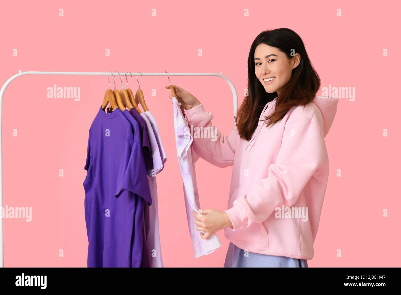 Young Asian woman and rack with t-shirts on pink background Stock Photo ...