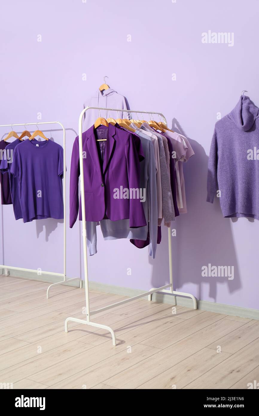 Racks with clothes in purple shades near lilac wall Stock Photo - Alamy