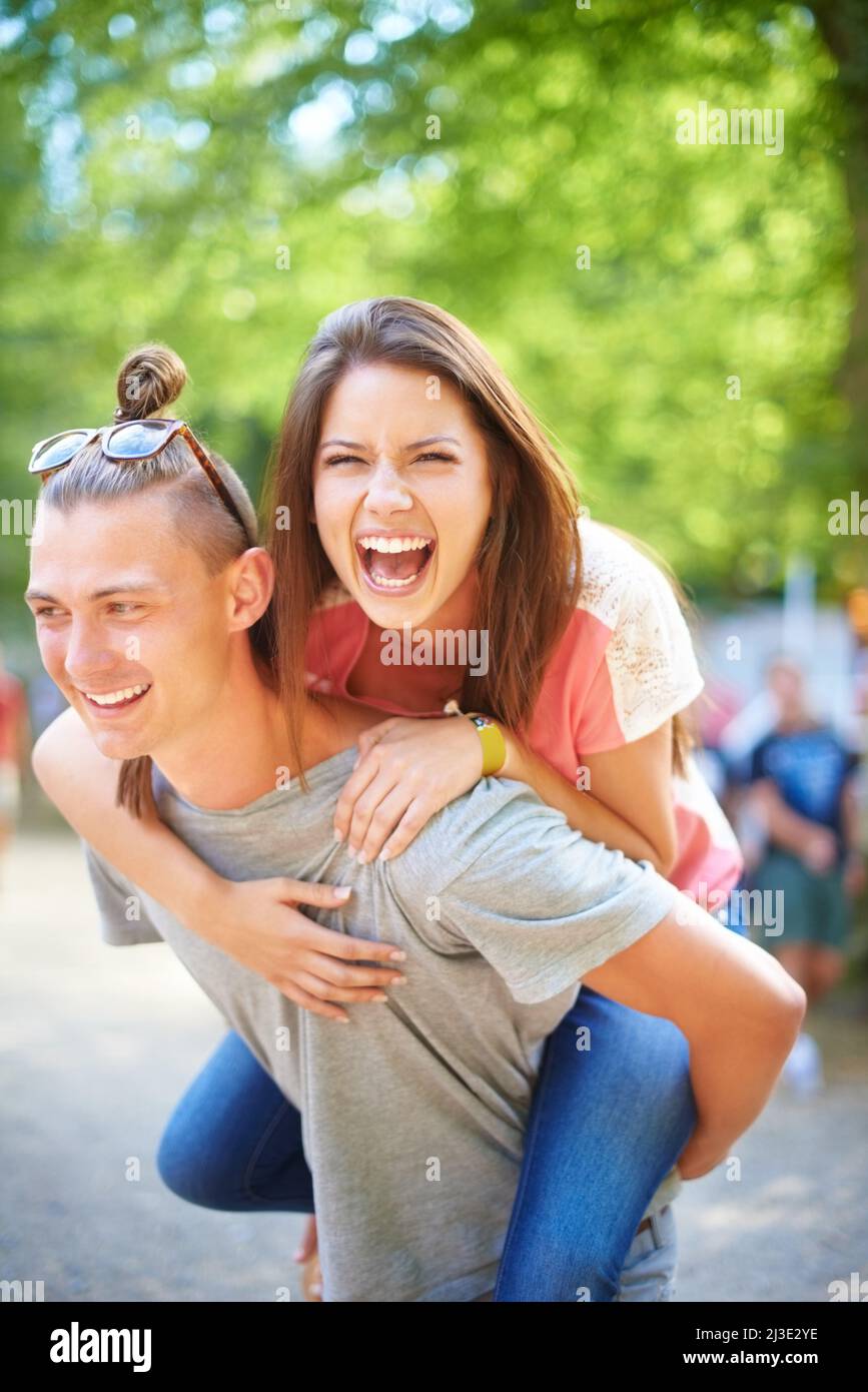 Young love. A trendy young man giving his girlfriend a piggyback ride ...