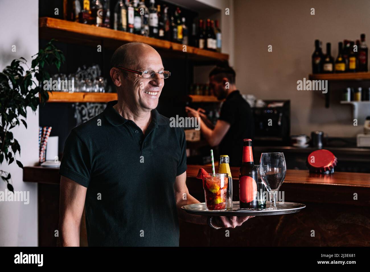 Mature, smiling waiter holding a tray with his hands. Worker in his ...