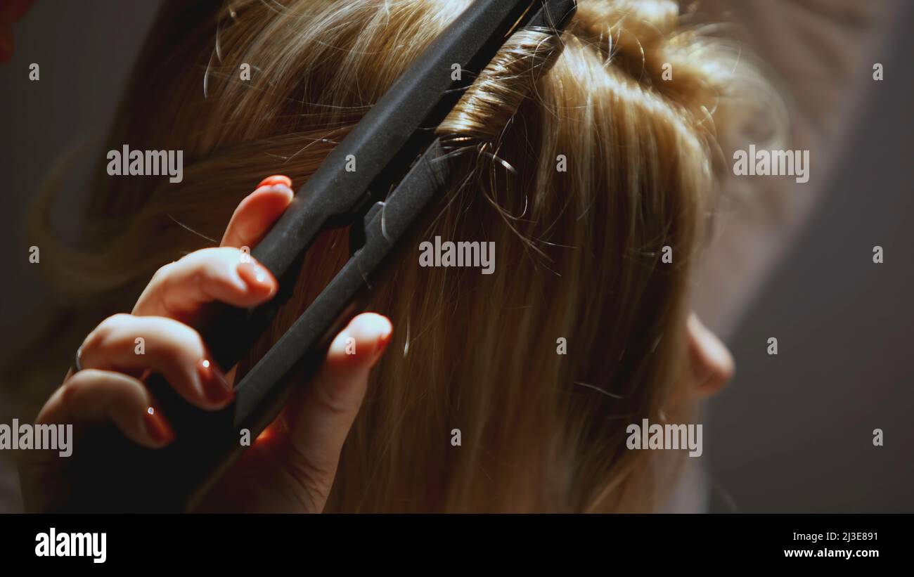 The girl winds curls on a curling iron. ART. The girl has blond hair ...