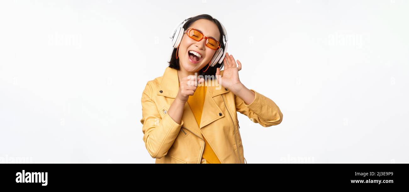 Beautiful asian girl, laughing happy, listening music in headphones ...