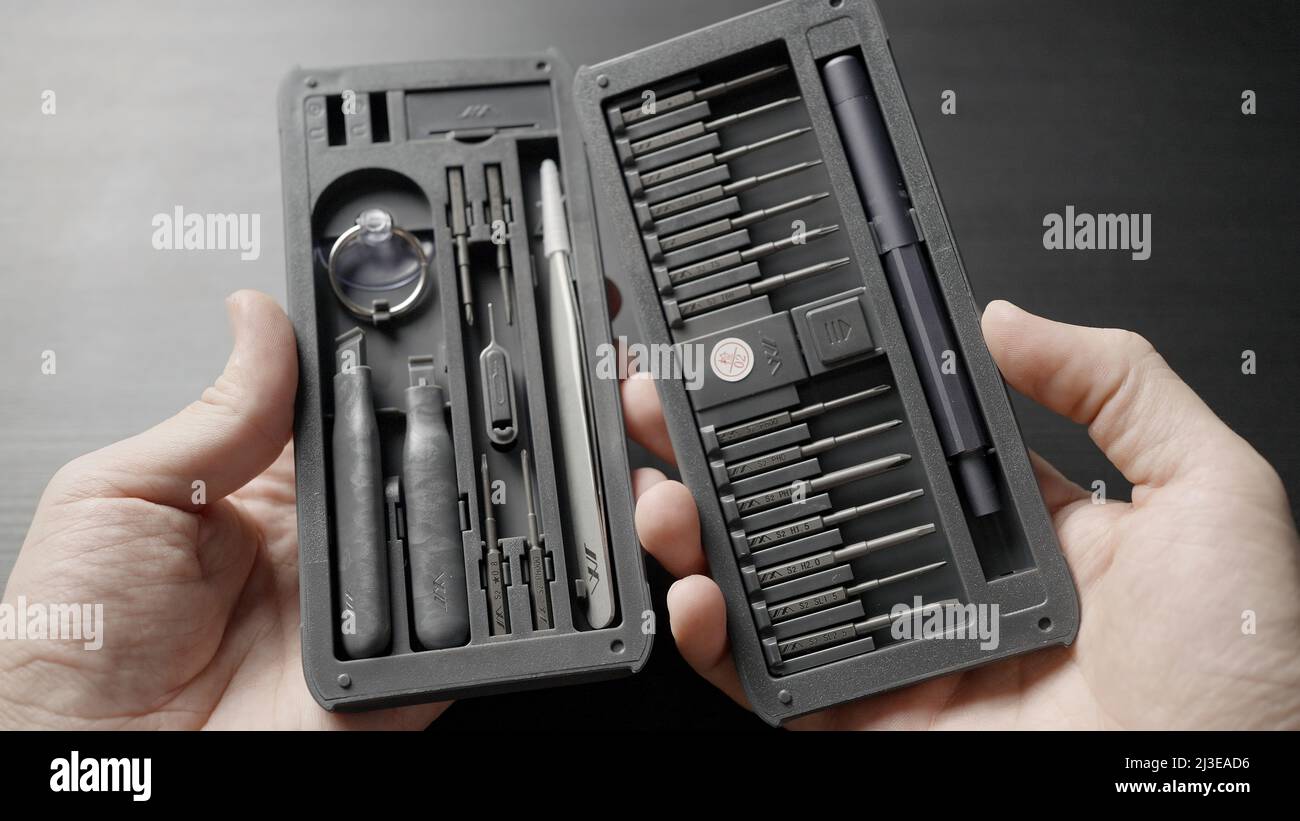 Set of screwdrivers with gray handles in a box in male hands on a dark ...