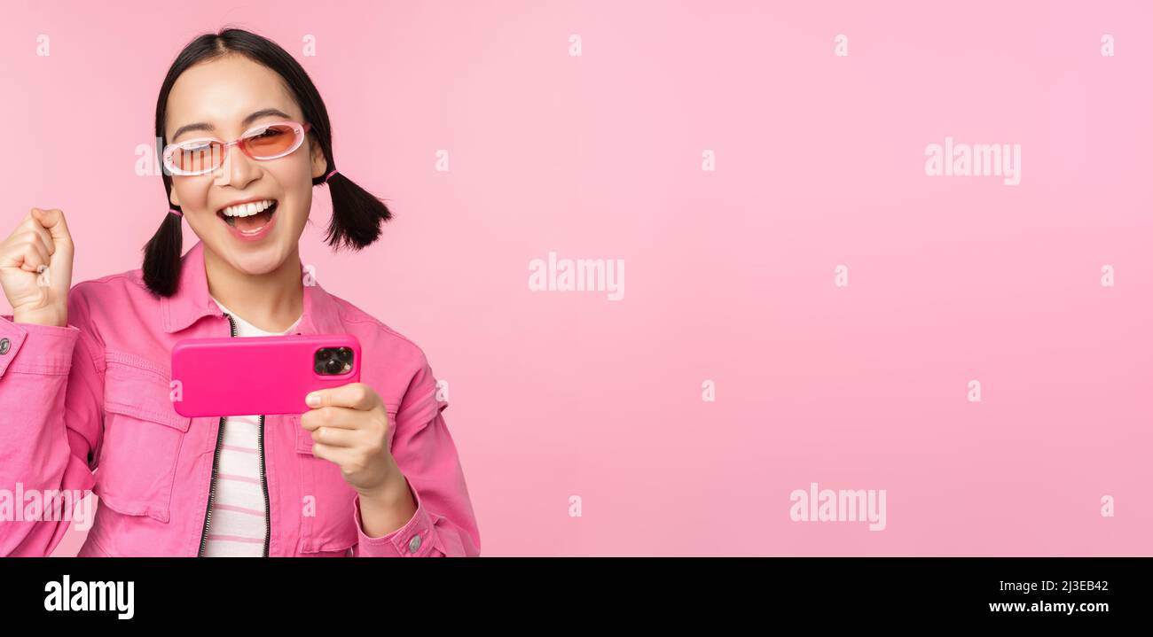 Happy smiling korean girl winning on mobile phone, looking at ...