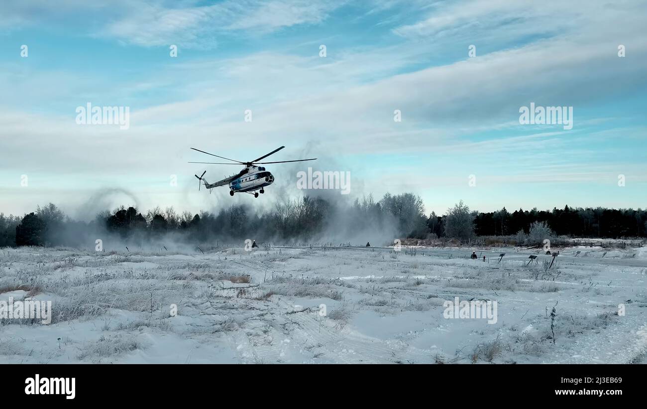 Helicopter landing on a snowy field with the forest and cloudy sky on ...