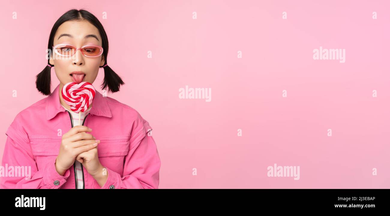 Silly and cute asian female model licking lolipop, eating candy sweet ...