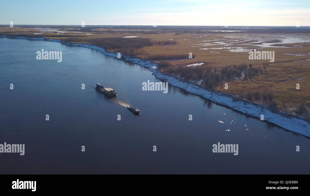 Aerial view of a barge floating on a wide river past the autumn meadows ...
