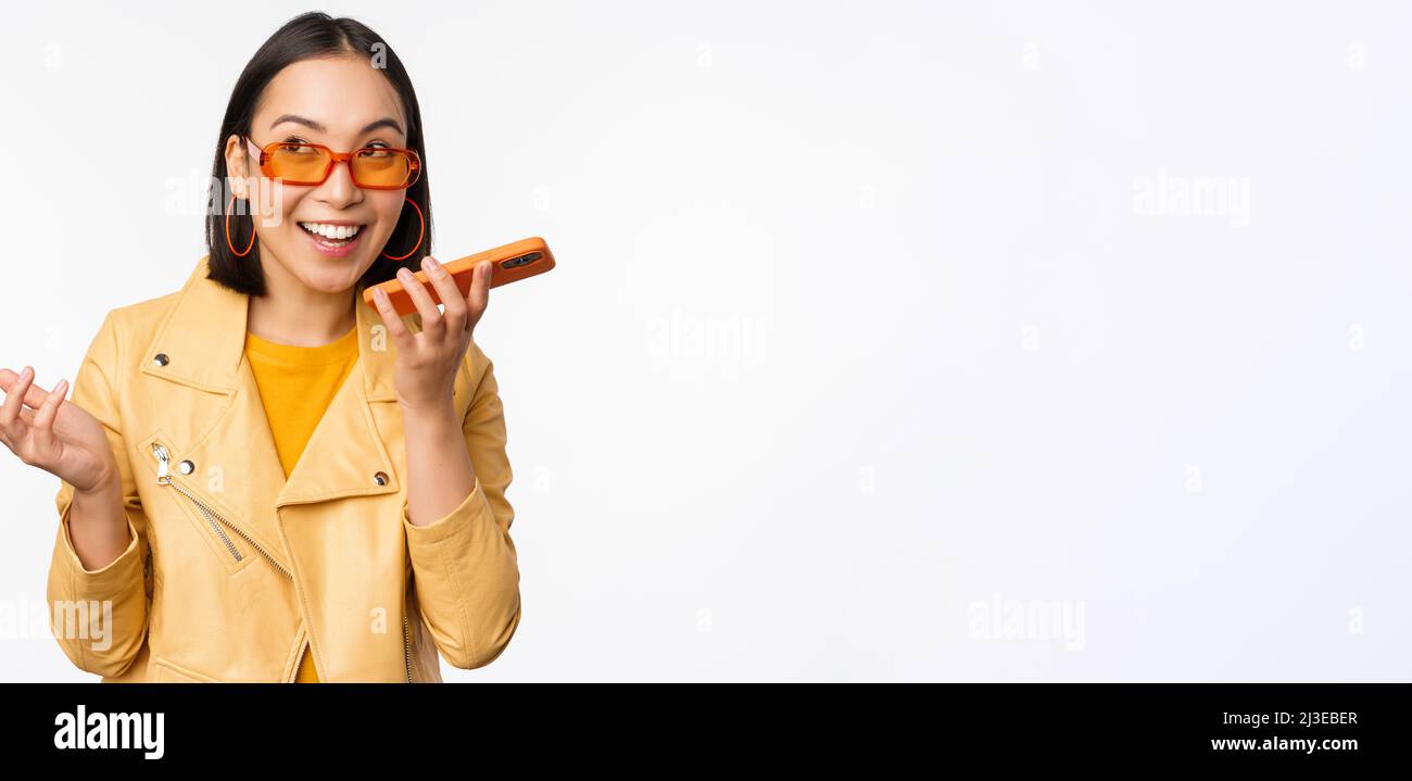 Image of happy asian girl talking on speakerphone, recording ...