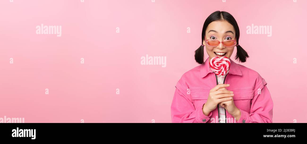 Silly and cute asian female model licking lolipop, eating candy sweet ...