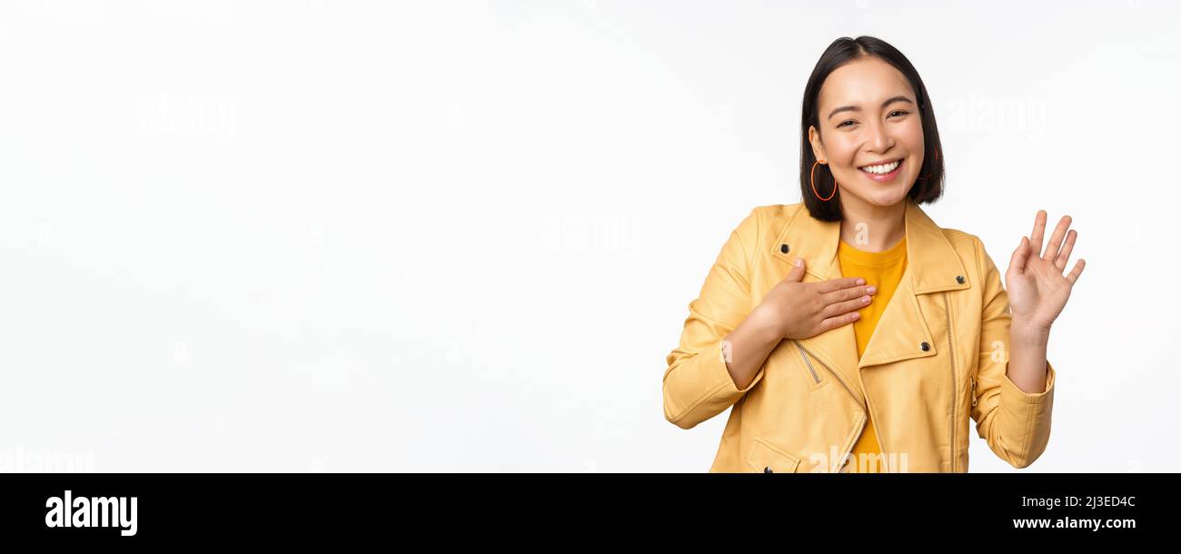 Image of friendly asian girl in stylish yellow coat, raising arm ...