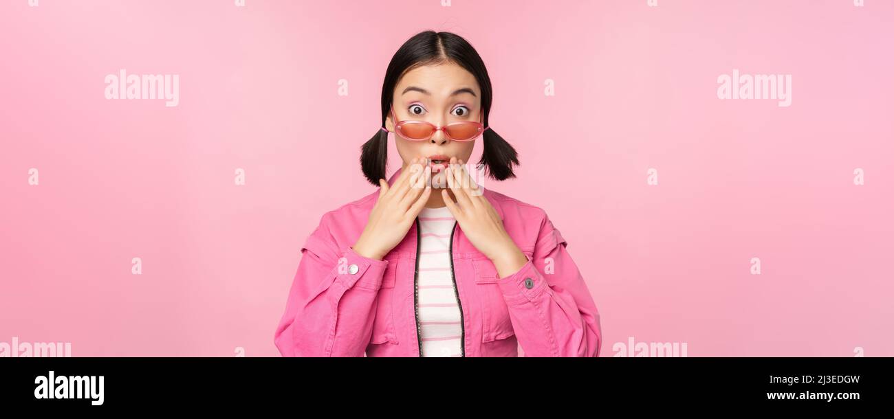 Portrait of young asian woman in stylish sunlgasses, looking surprised ...