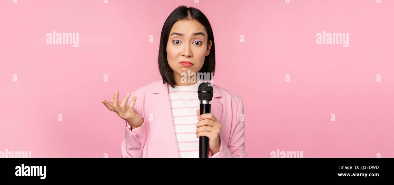 Indecisive, nervous asian business woman holding mic, shrugging and ...