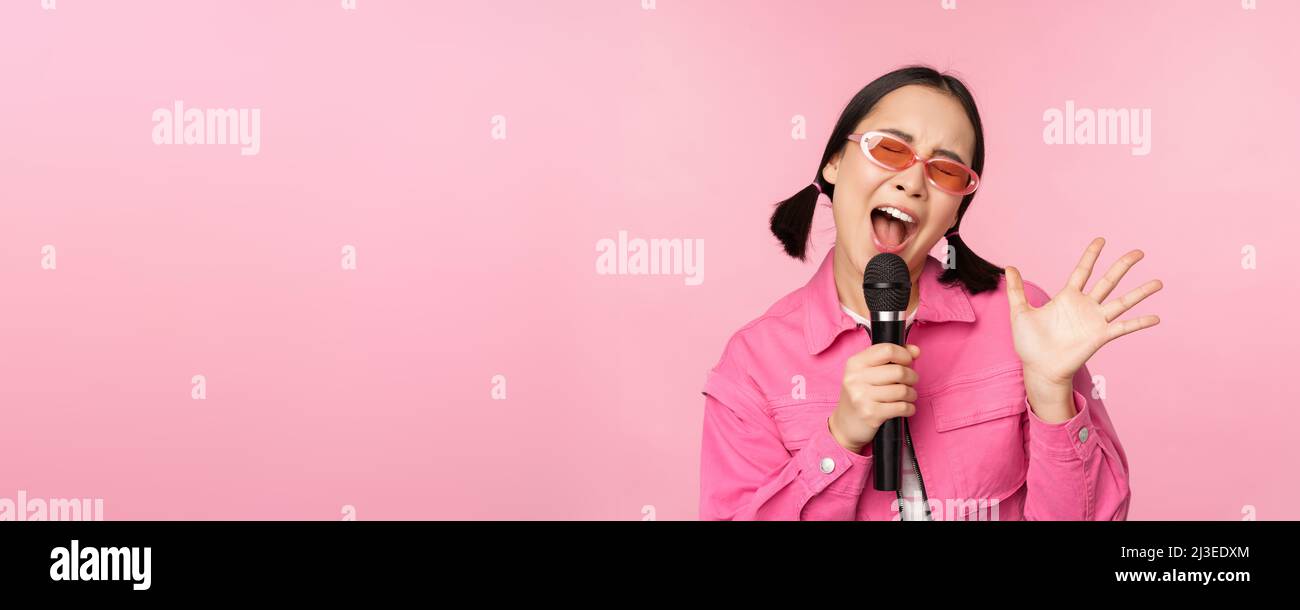 Happy beautiful asian girl singing with mic, using microphone, enjoying ...
