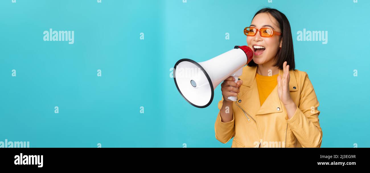 Stylish asian girl making announcement in megaphone, shouting with ...