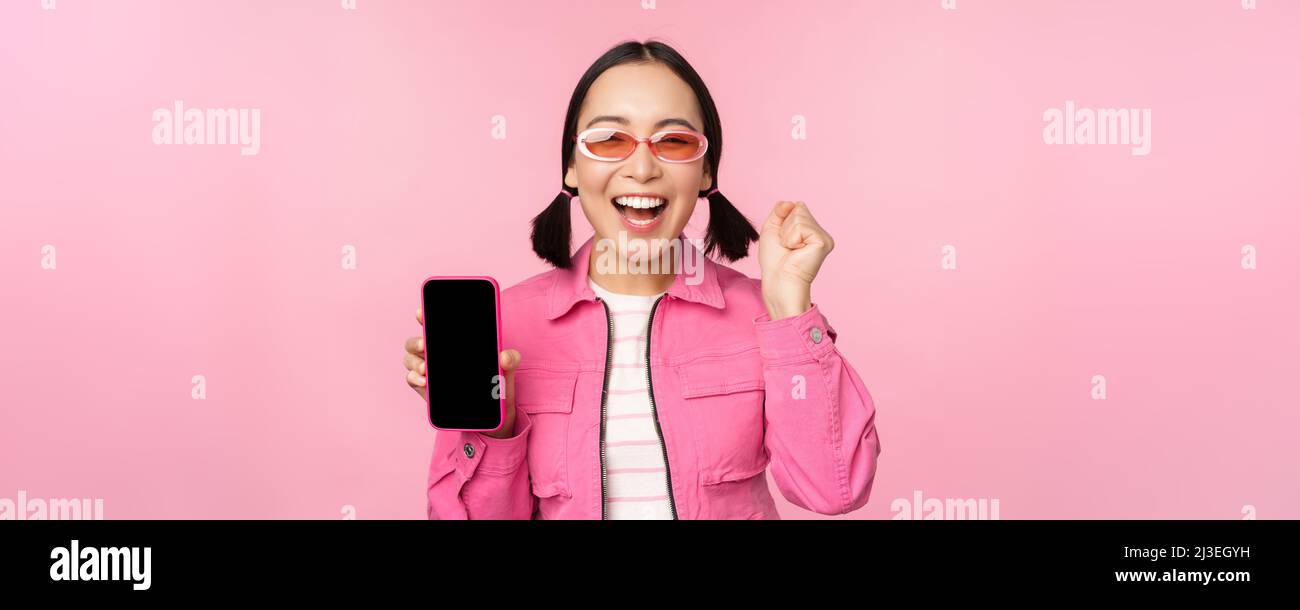 Excited asian girl laughs and smiles, shows mobile phone screen ...