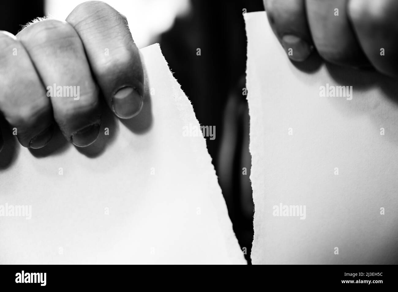 Two hands tearing a single blank sheet of paper from top to bottom ...