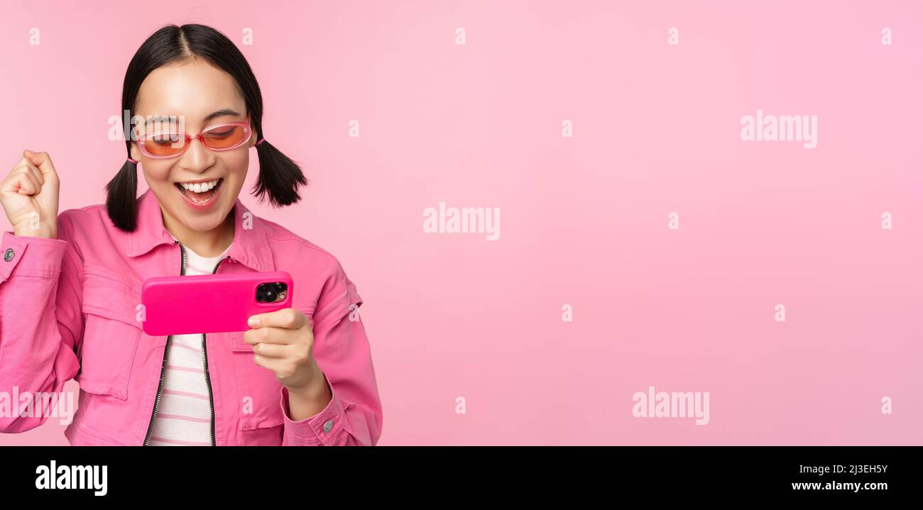 Happy smiling korean girl winning on mobile phone, looking at ...