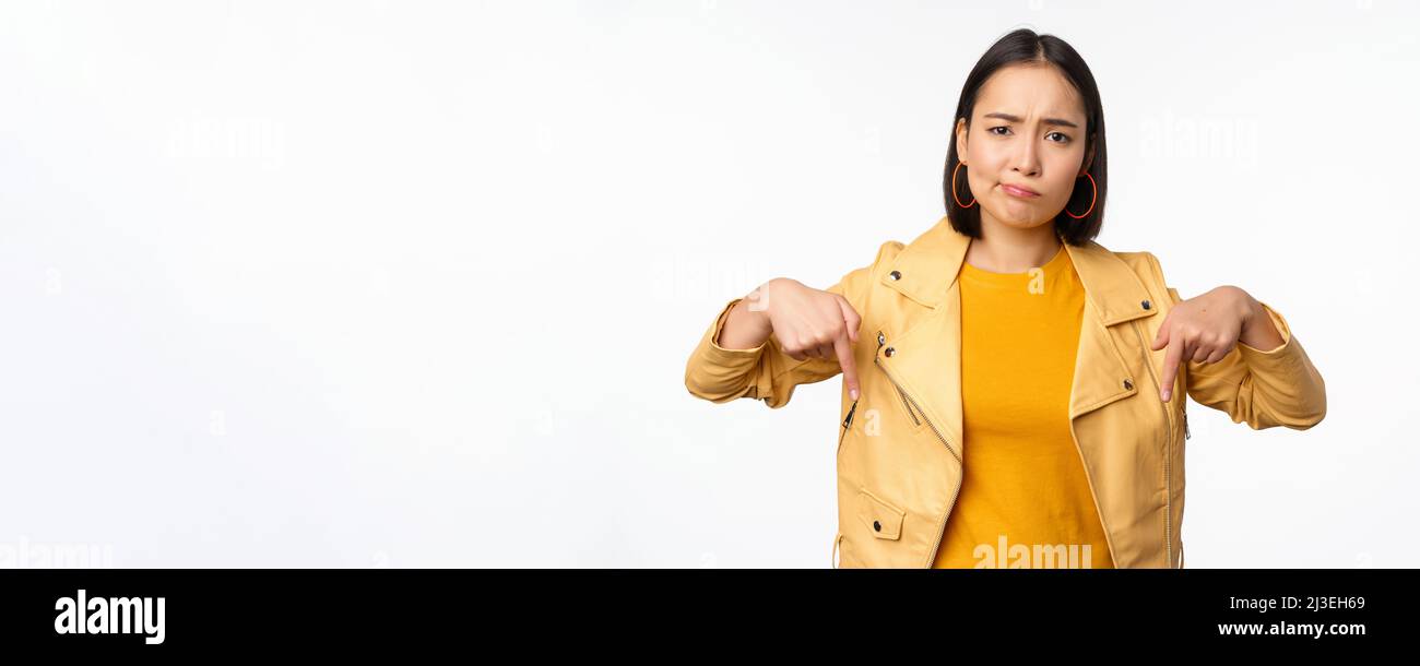 Portrait of disappointed asian woman pointing fingers down, grimacing ...