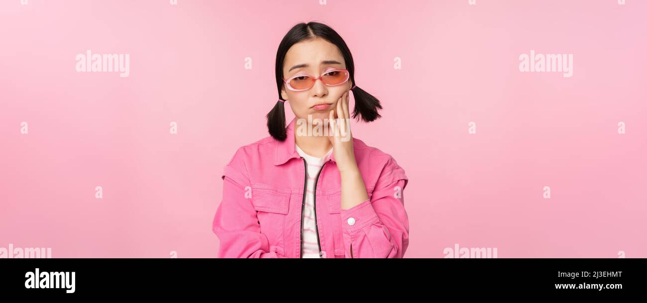 Image of sad asian girl sulking, touching her cheek, pouting ...