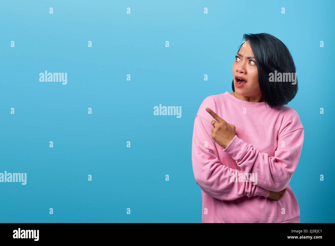 Attractive asian woman shocked and pointing finger to empty space on ...