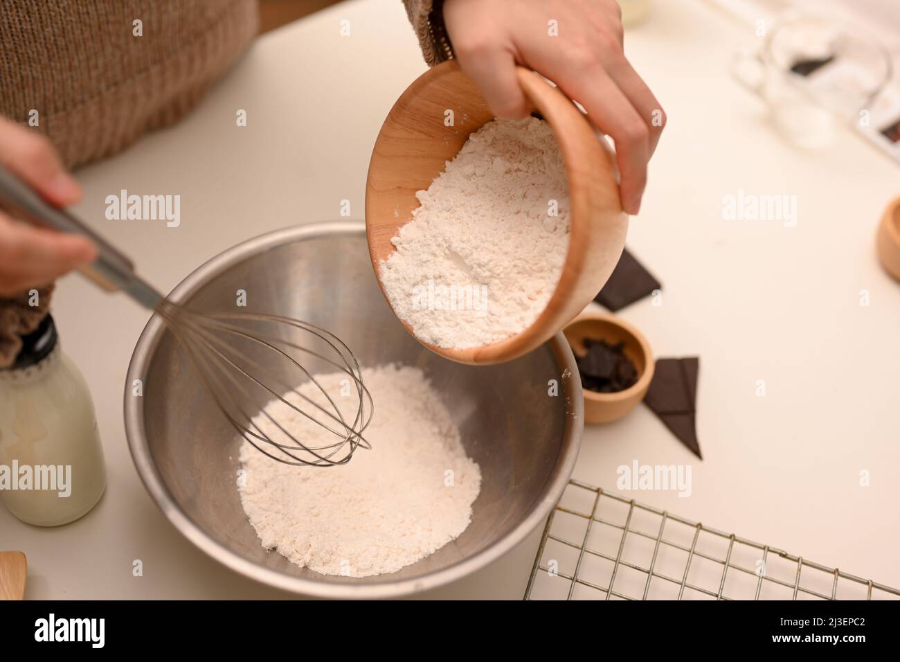 Female chef pouring a cup of flour into a mixing bowl, preparing the ...
