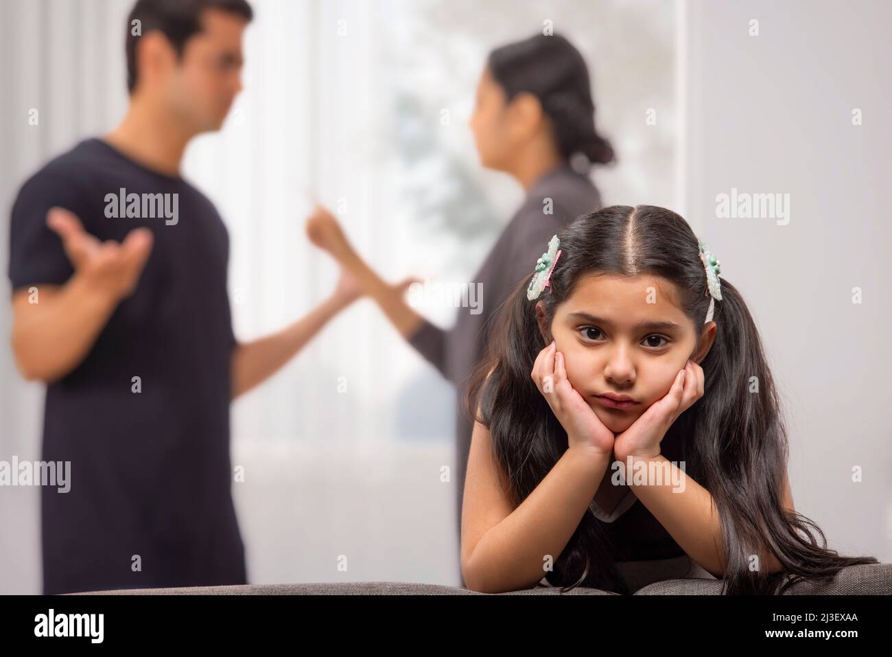 Portrait of a sad girl child with hands on cheek and parent arguing ...