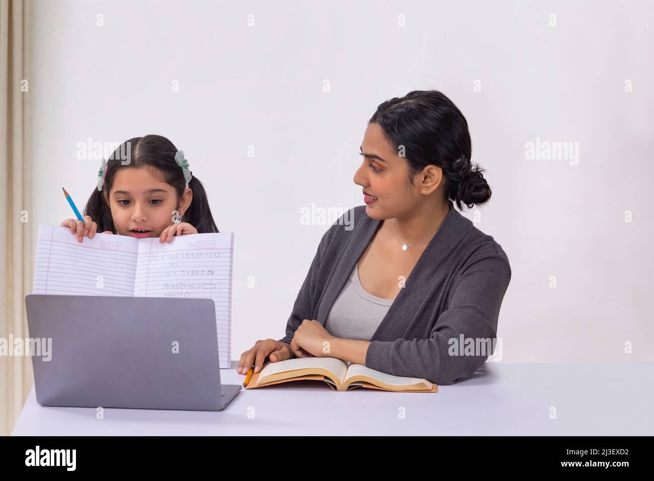 Girl submitting homework through online class using laptop and mother sitting beside Stock Photo ...