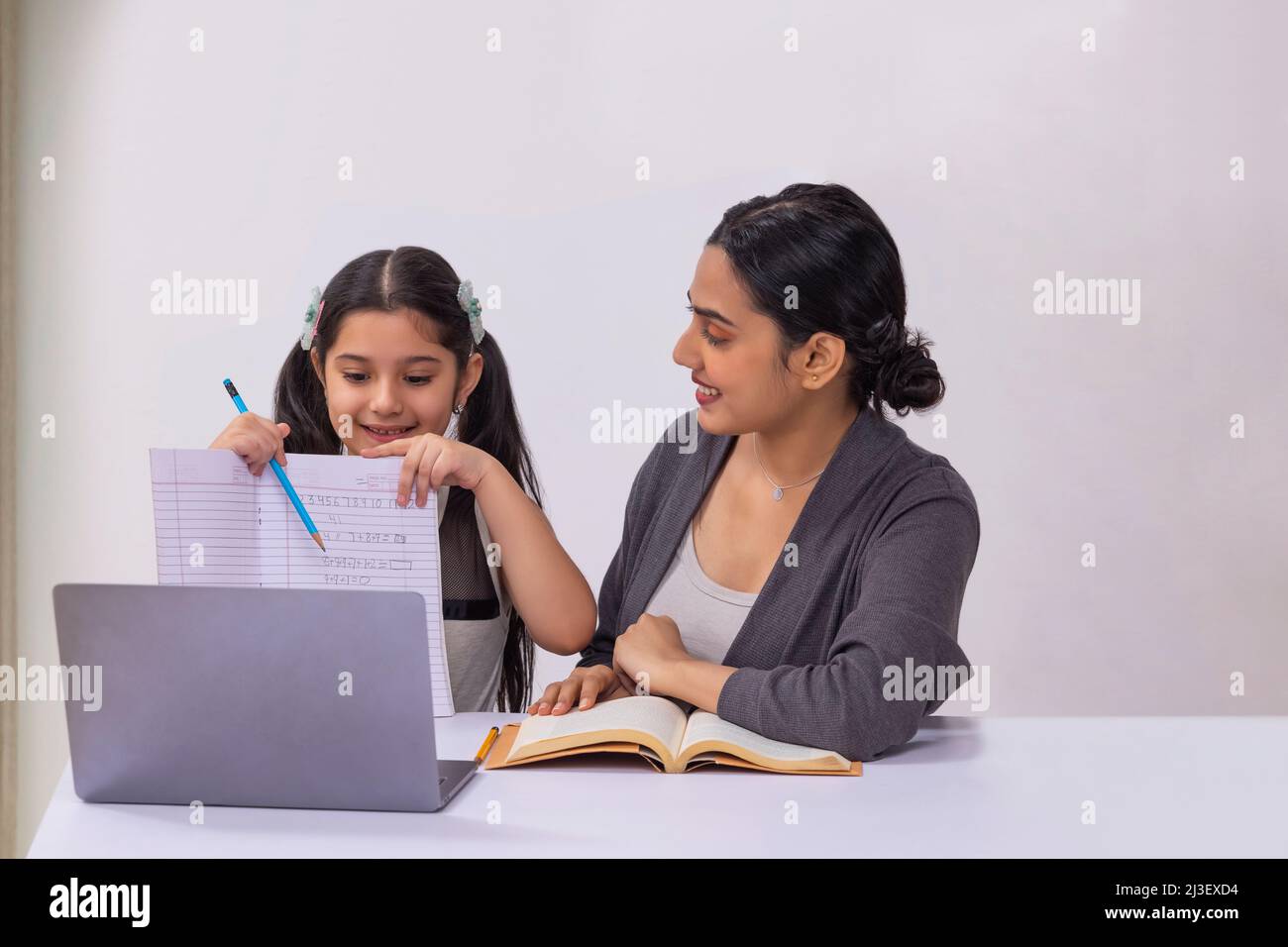 Girl submitting homework through online class using laptop and mother sitting beside Stock Photo ...
