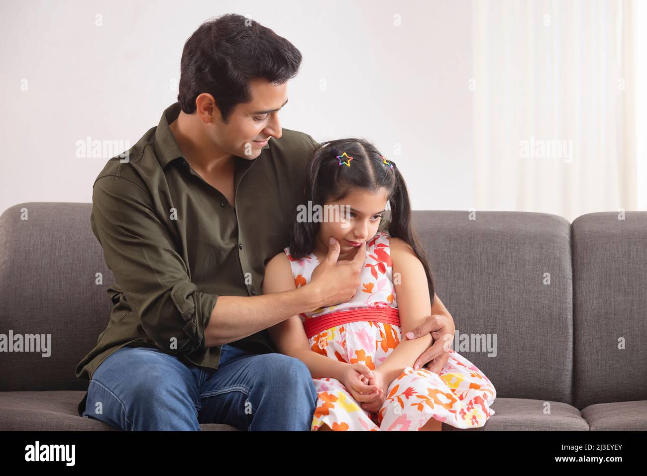 Father trying to control his daughter's anger while sitting on sofa ...