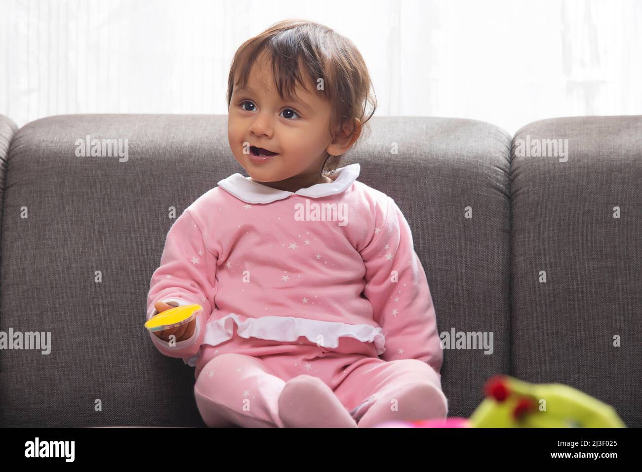 Cute baby with toy in hand looking away Stock Photo - Alamy