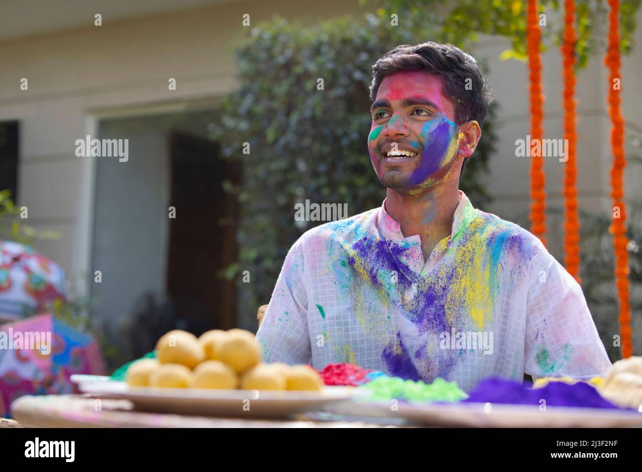 Portrait happy young man looking elsewhere with colourful face on Holi ...