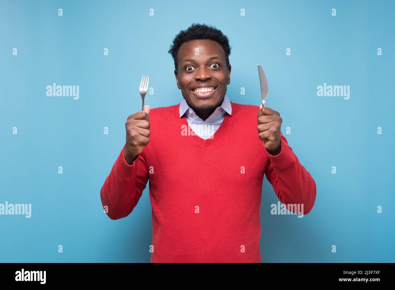 Hungry african young man holding fork and knife on hand ready to eat ...
