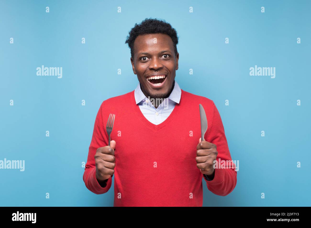 Hungry african young man holding fork and knife on hand ready to eat ...