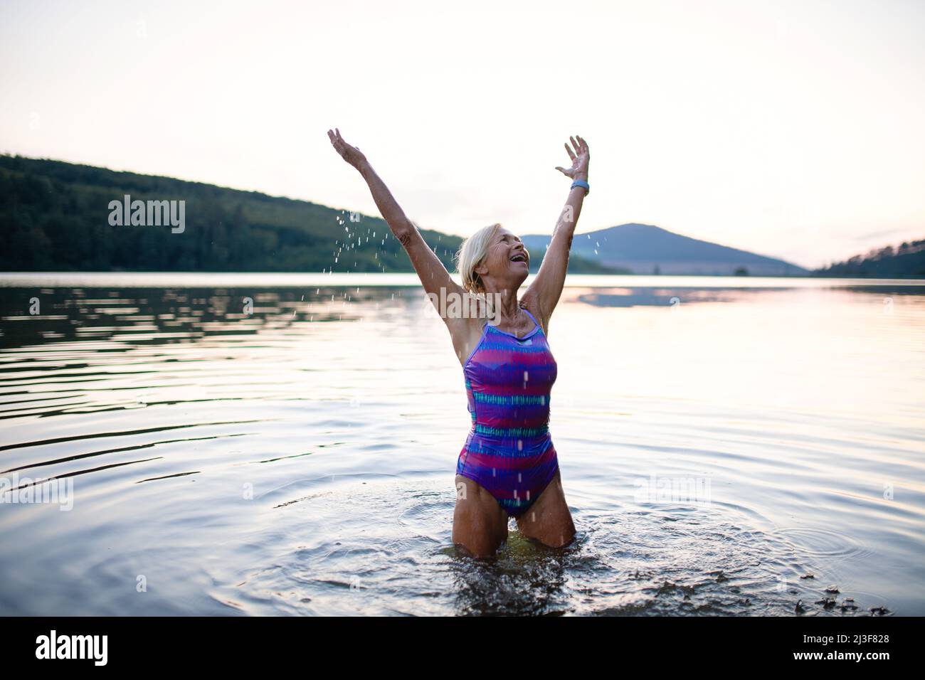 Portrait of active senior woman swimmer standing and stretching ...