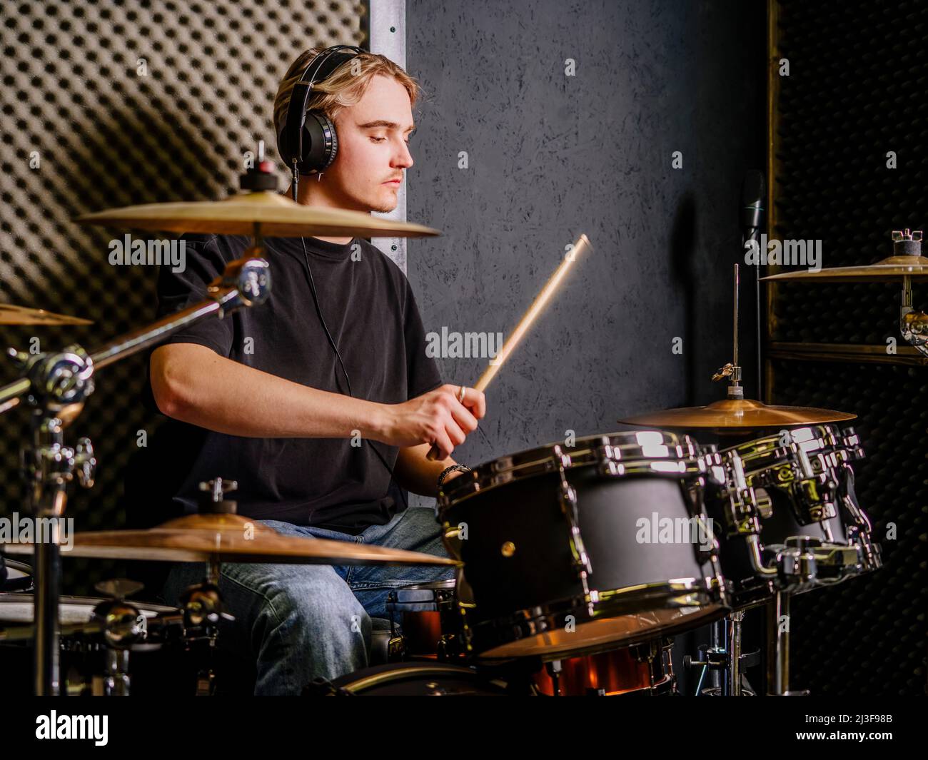 Young man wearing headphones and playing drums in a recording studio ...