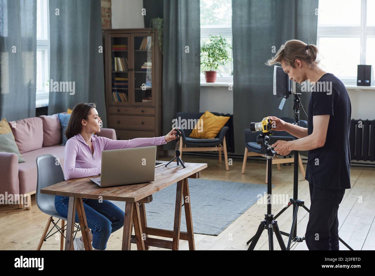 Male operator standing at tripod and using camera while shooting ...