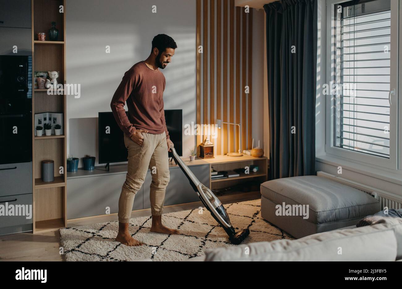 Young man hoovering carpet with vacuum cleaner in living room Stock ...