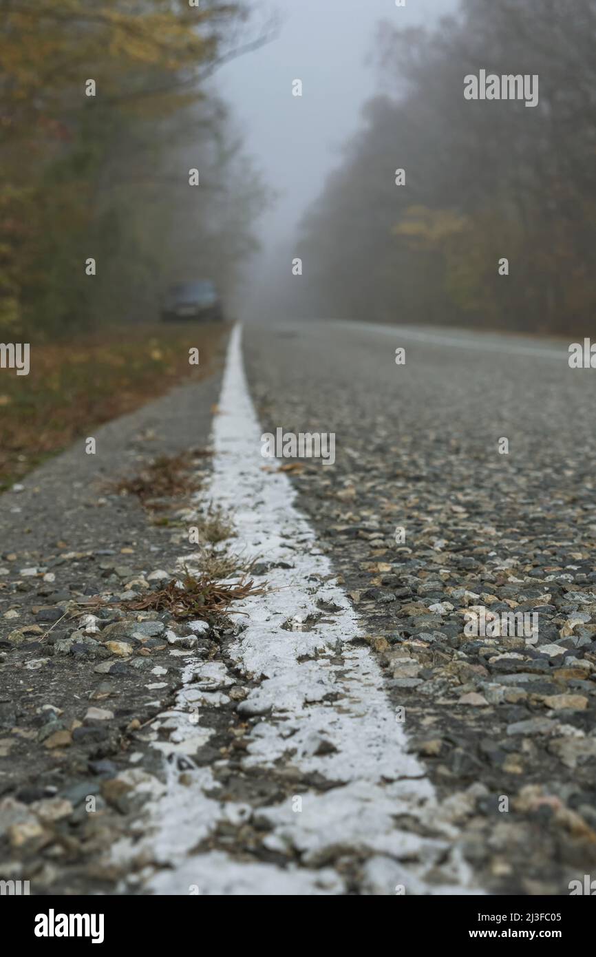 A cracked white solid line by the side of the asphalt road going into ...