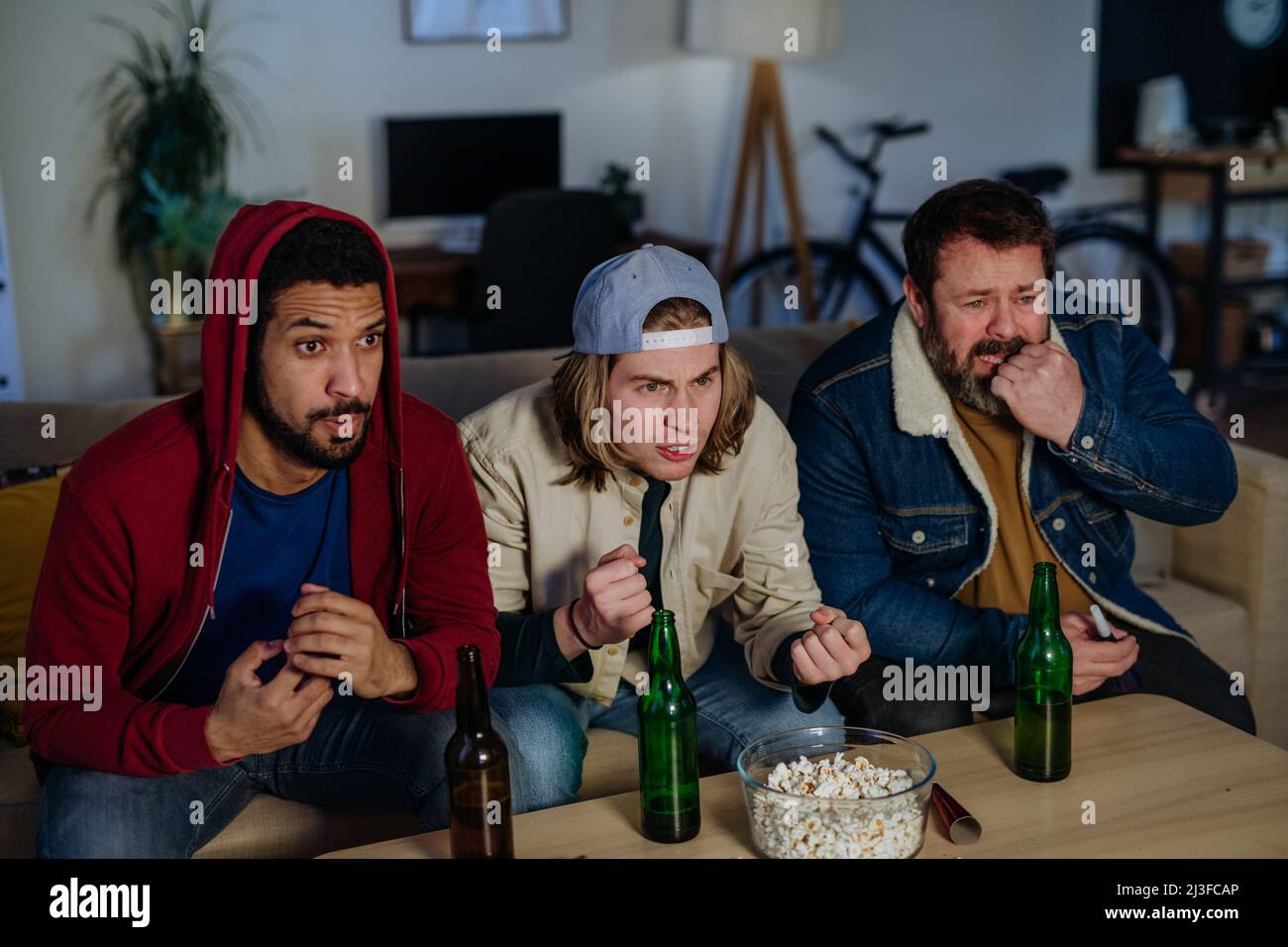 Nervous football fans friends watching live soccer match on TV at home ...