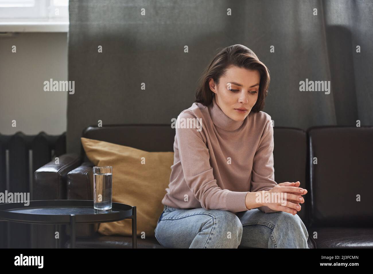 Dejected young Caucasian woman with brown hair sitting on sofa and ...