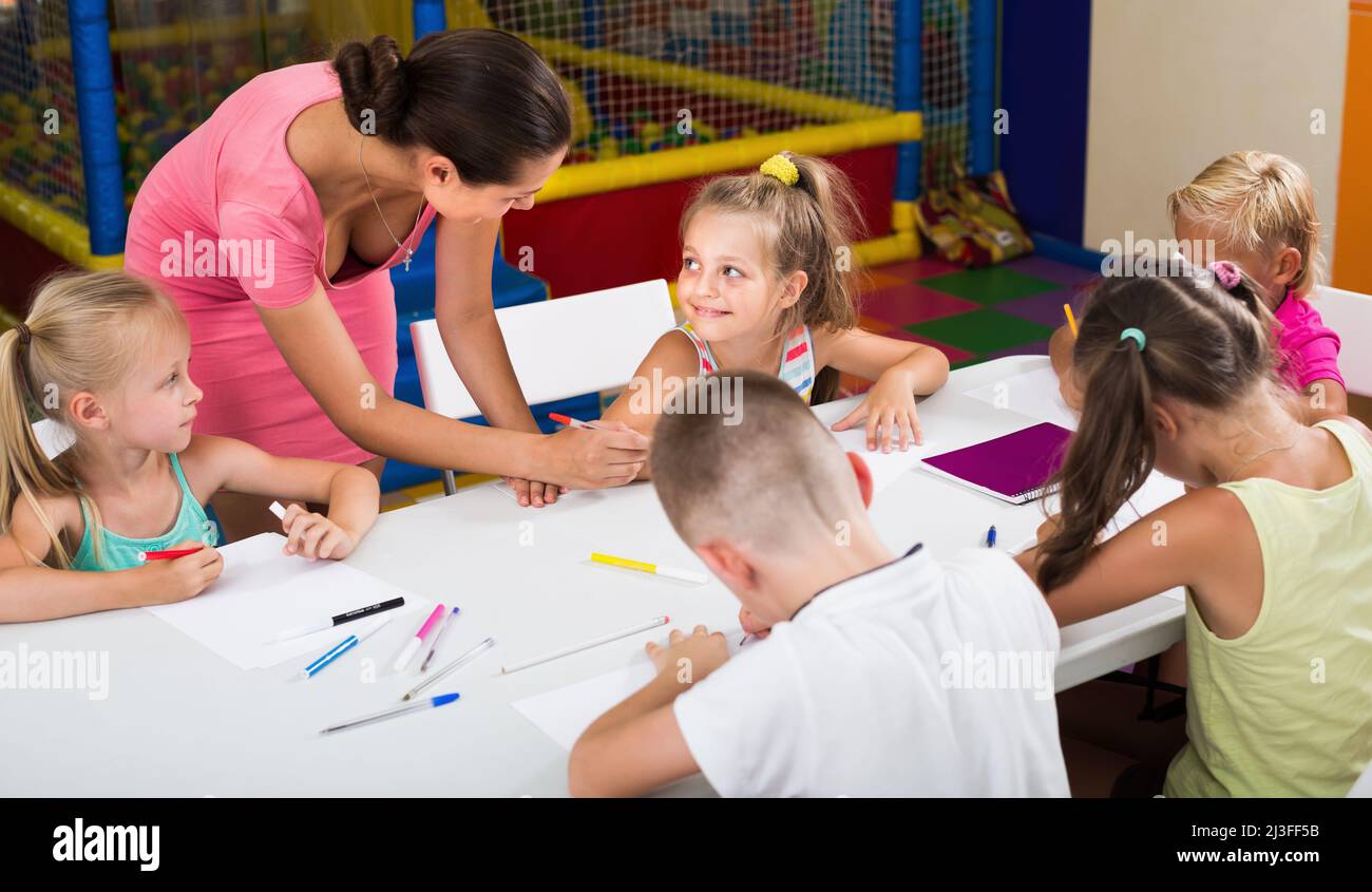 Glad girl and kids drawing on lesson with help of teacher Stock Photo ...