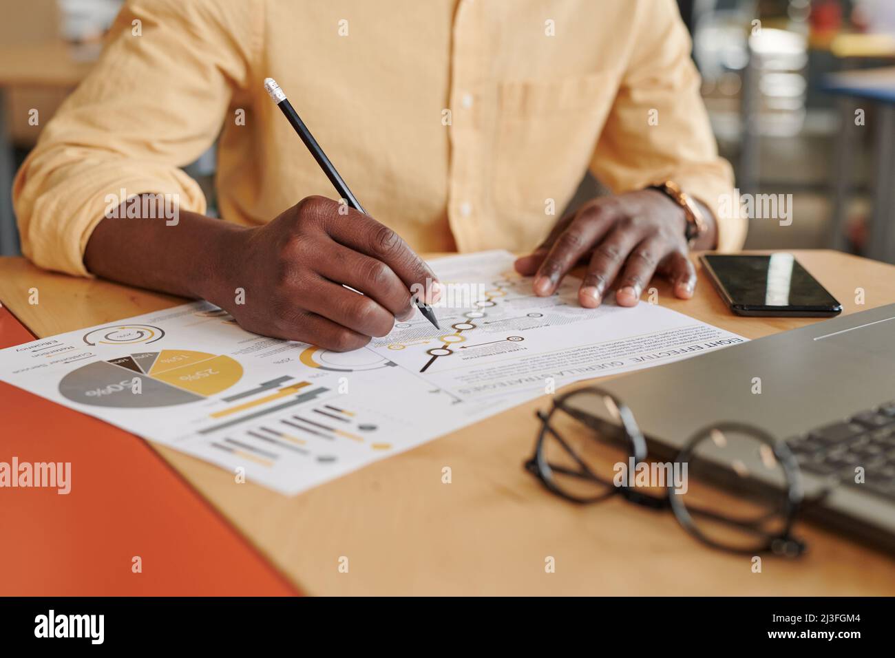 Close-up of unrecognizable black manager sitting at table and editing ...