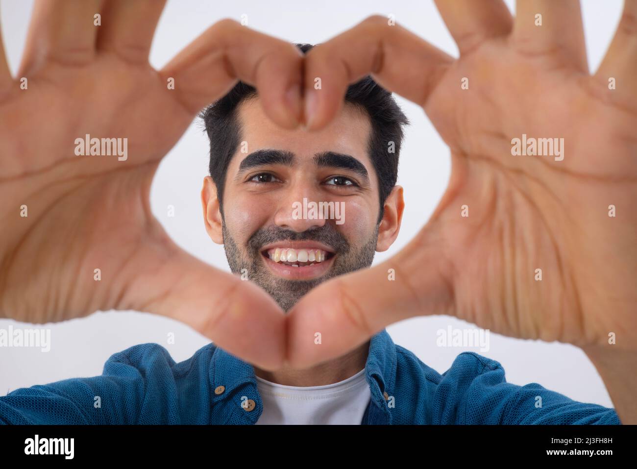 Adult man forming heart shape with her fingers and looking at camera ...