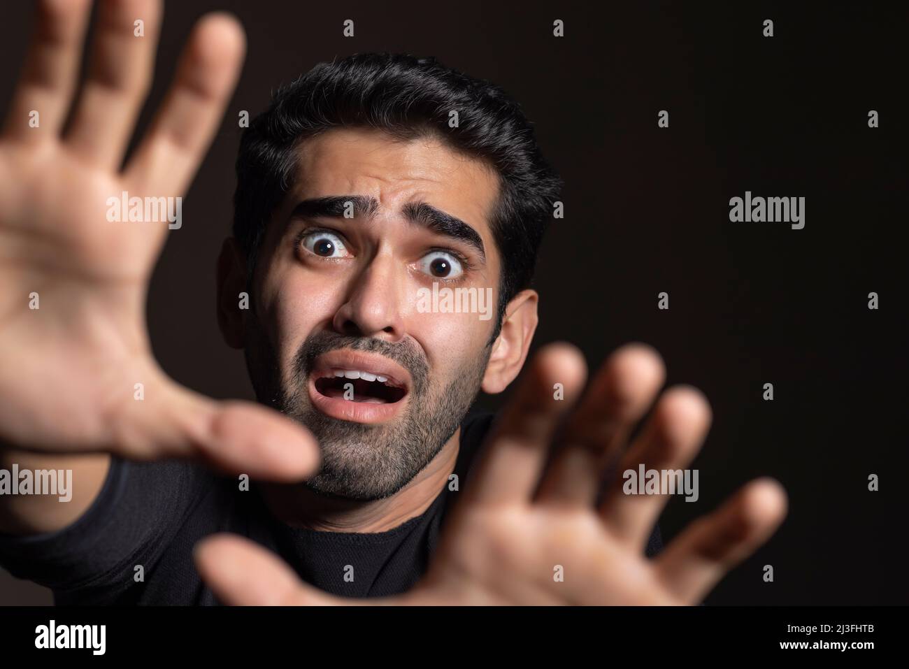 Portrait of a frightened young man looking at the camera and gesturing ...
