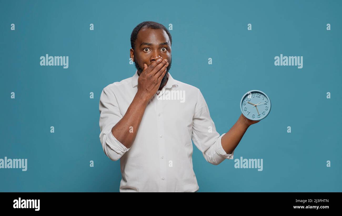 Shocked man checking time on clock and running late to work, looking at ...