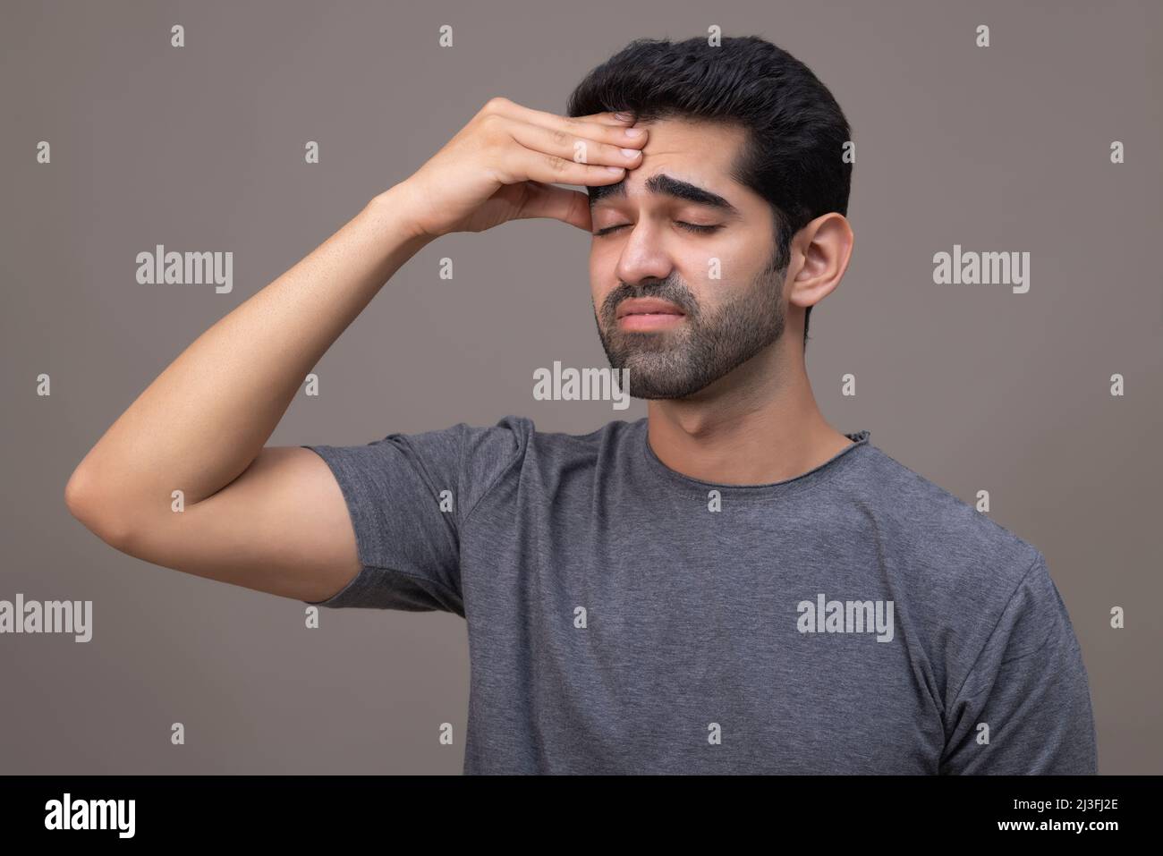 Portrait of a young man suffering from headache with hand on forehead ...