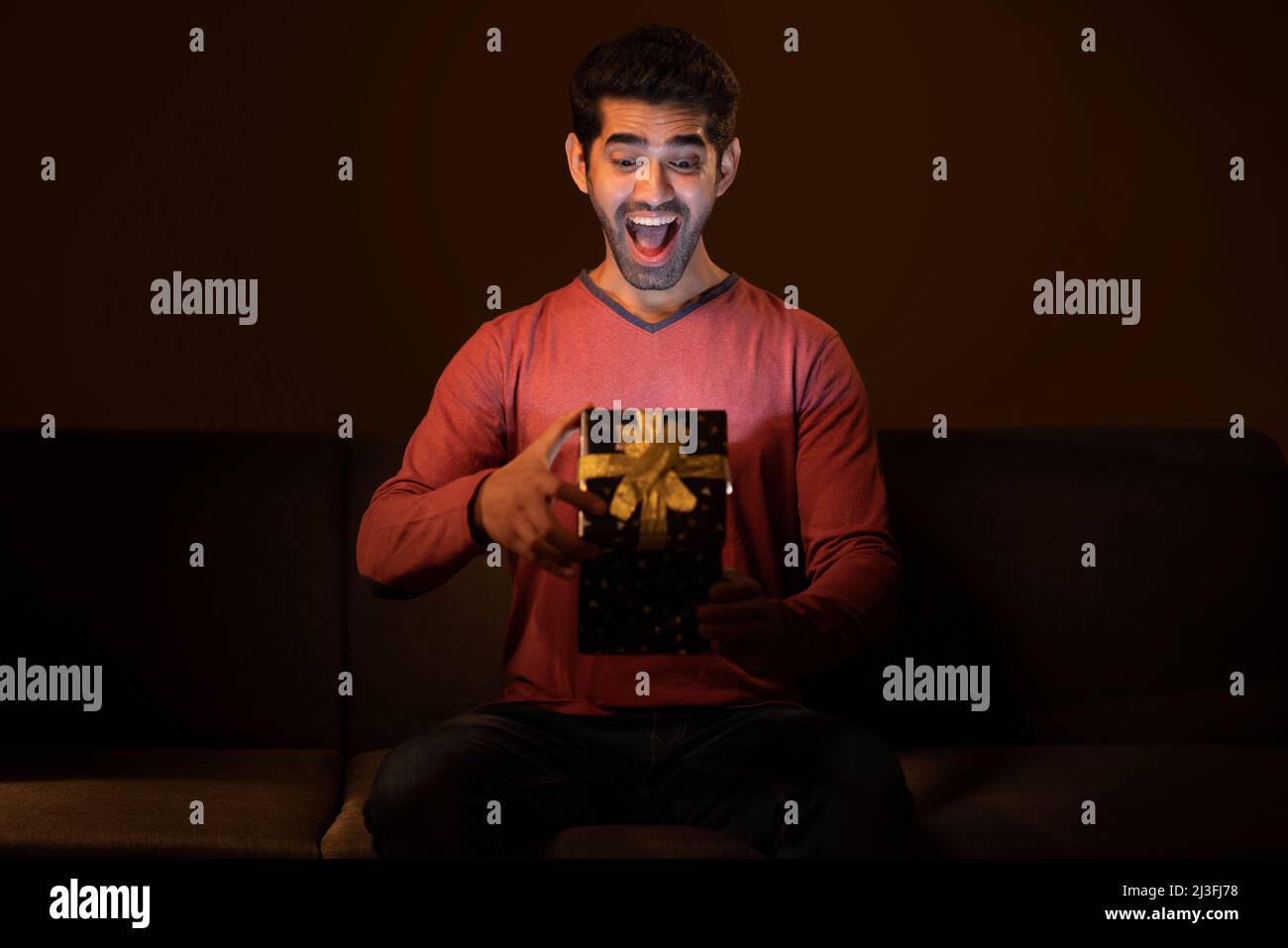 Happy young man unpacking gift box with curiosity Stock Photo - Alamy