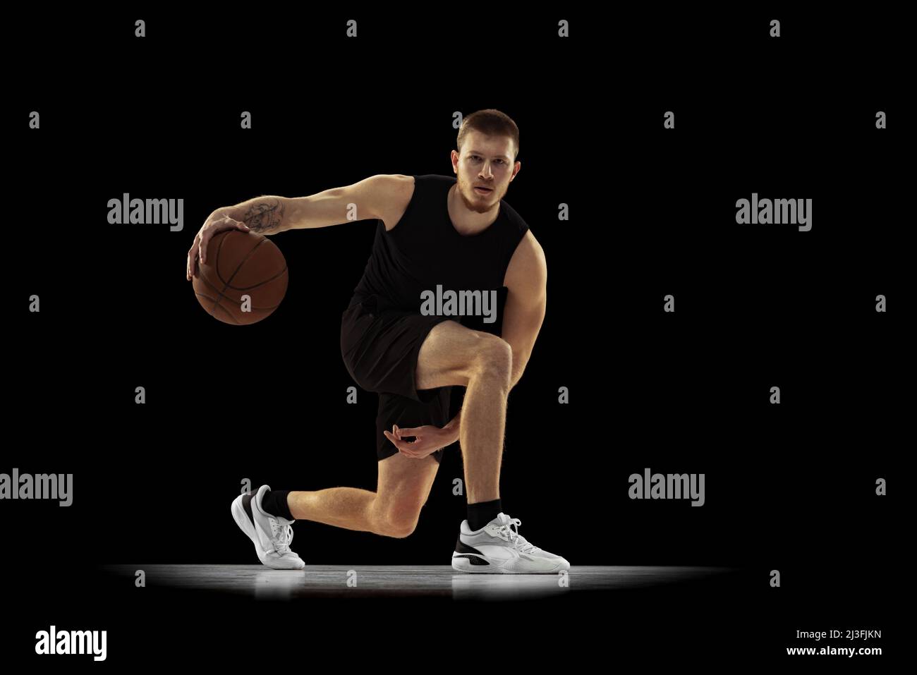 Ground move. Dynamic portrait of young man, basketball player in black ...